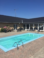 Piscina retangular com escadas de metal, cercada por um alpendre de tijolos.