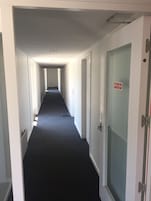 Um corredor estreito com carpete preto, paredes brancas e uma porta com a placa Brandner.