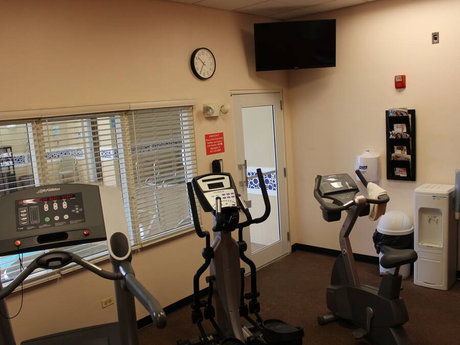 Centro de fitness com equipamentos de cardio, relógio e bebedouro.