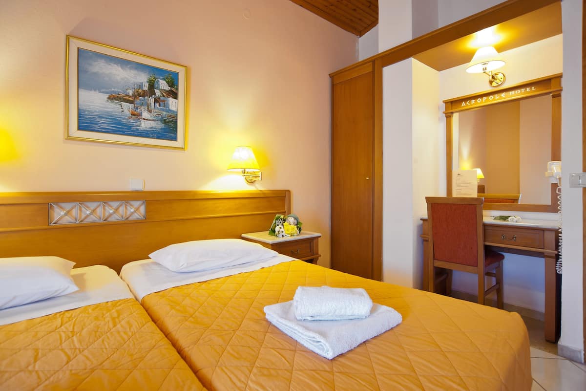 Quarto de hotel com duas camas, um quadro, uma escrivaninha e um espelho.