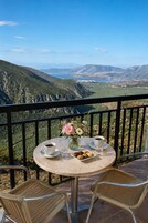 Terraço com mesa posta para dois, com vista para uma paisagem montanhosa.