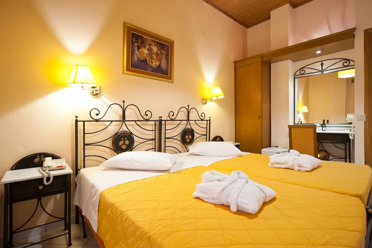 Quarto de hotel com duas camas, uma mesinha de cabeceira com um telefone, um quadro na parede e um espelho no canto.