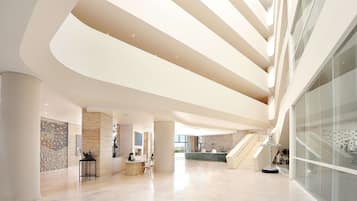 Um hall espaçoso com design moderno, com uma área de recepção central, uma escadaria e uma escultura decorativa.
