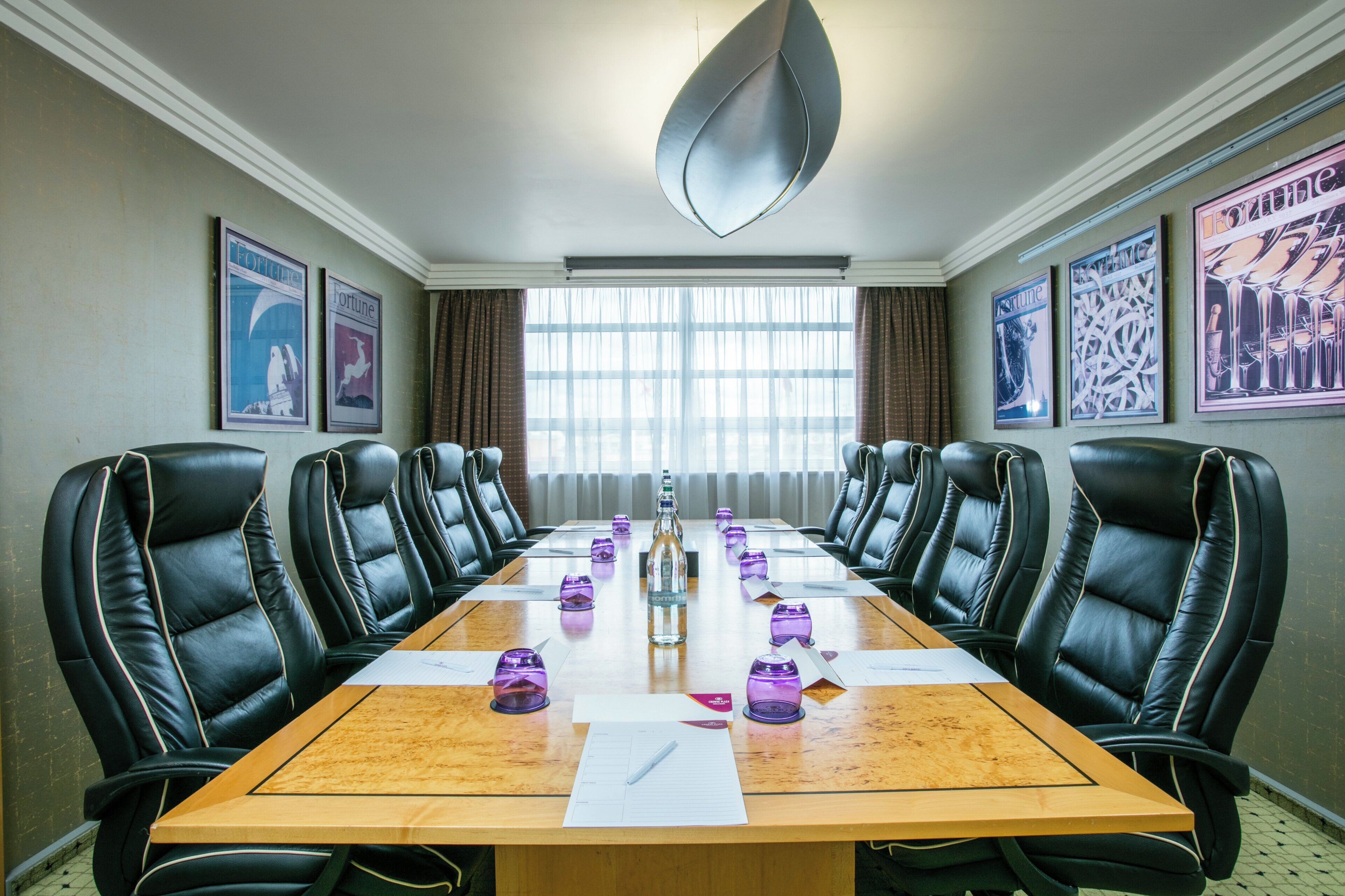 Sala de conferência com uma mesa comprida, cadeiras de couro preto e copos de vidro roxos.