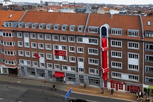 Um hotel com vários andares, telhados de telha vermelha e uma placa vermelha em destaque indicando ser o Hotel Gestus.