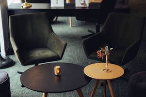 Quarto moderno com duas cadeiras verde-escuro, uma mesa redonda com uma vela e uma mesa pequena com um objeto decorativo.