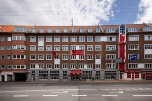 Um hotel com vários andares, fachada vermelha e branca, várias janelas e uma placa chamativa com o nome 'HOTEL GESTUS'.