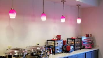 Uma cozinha com quatro luminárias pendentes, uma bancada com diversos eletrodomésticos e recipientes, e um porta-temperos fixado na parede.