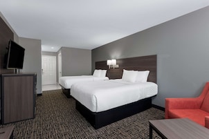 Quarto de hotel com duas camas, uma escrivaninha, uma televisão e uma cadeira vermelha.
