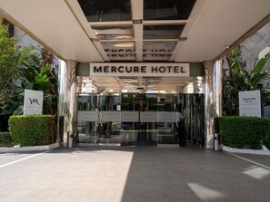 A entrada do Hotel Mercure, com design moderno, apresenta uma porta de vidro e uma placa acima.