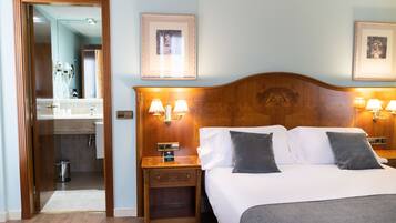 Quarto de hotel com cabeceira de madeira, duas luminárias de apoio, mesa de cabeceira com abajur, espelho e quadros na parede.