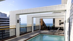 Piscina no terraço com vista para o oceano, cercada por paredes revestidas de azulejos e um guarda-corpo de vidro.