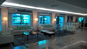 Ampla sala de estar com diversas opções de assento, grandes janelas com cortinas e um espaço de bar ao fundo.