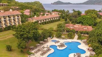Resort com uma piscina grande, vários edifícios e vegetação exuberante.