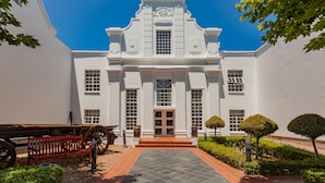 Um edifício branco com uma entrada central, ladeada por colunas, e um relógio sobre a porta.