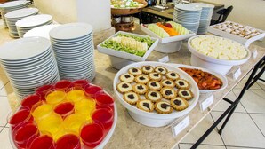 Buffet com diversos alimentos e pratos empilhados.