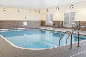 Piscina com deck ladrilhado, sala de trocas com banheiro e área de estar com cadeiras.
