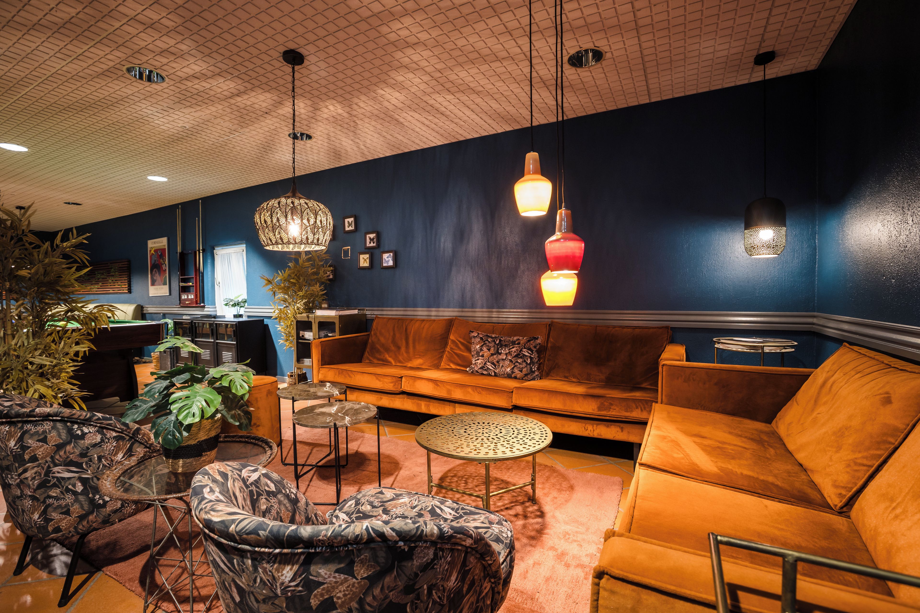 Espaço de estar moderno com parede azul, sofá laranja, poltronas estampadas e mesa de centro redonda.