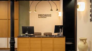 Um balcão de recepção com dois monitores, uma bancada de madeira e uma parede com o texto 'PRECIAOS PETITPALACE'.
