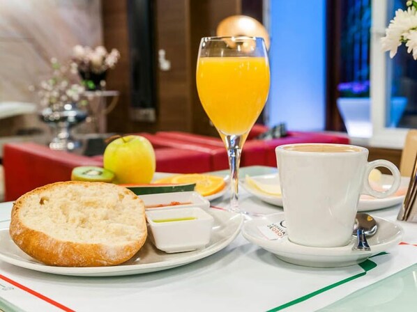 Uma mesa posta para o café da manhã, com torradas, frutas, um copo de suco de laranja e uma xícara de café.