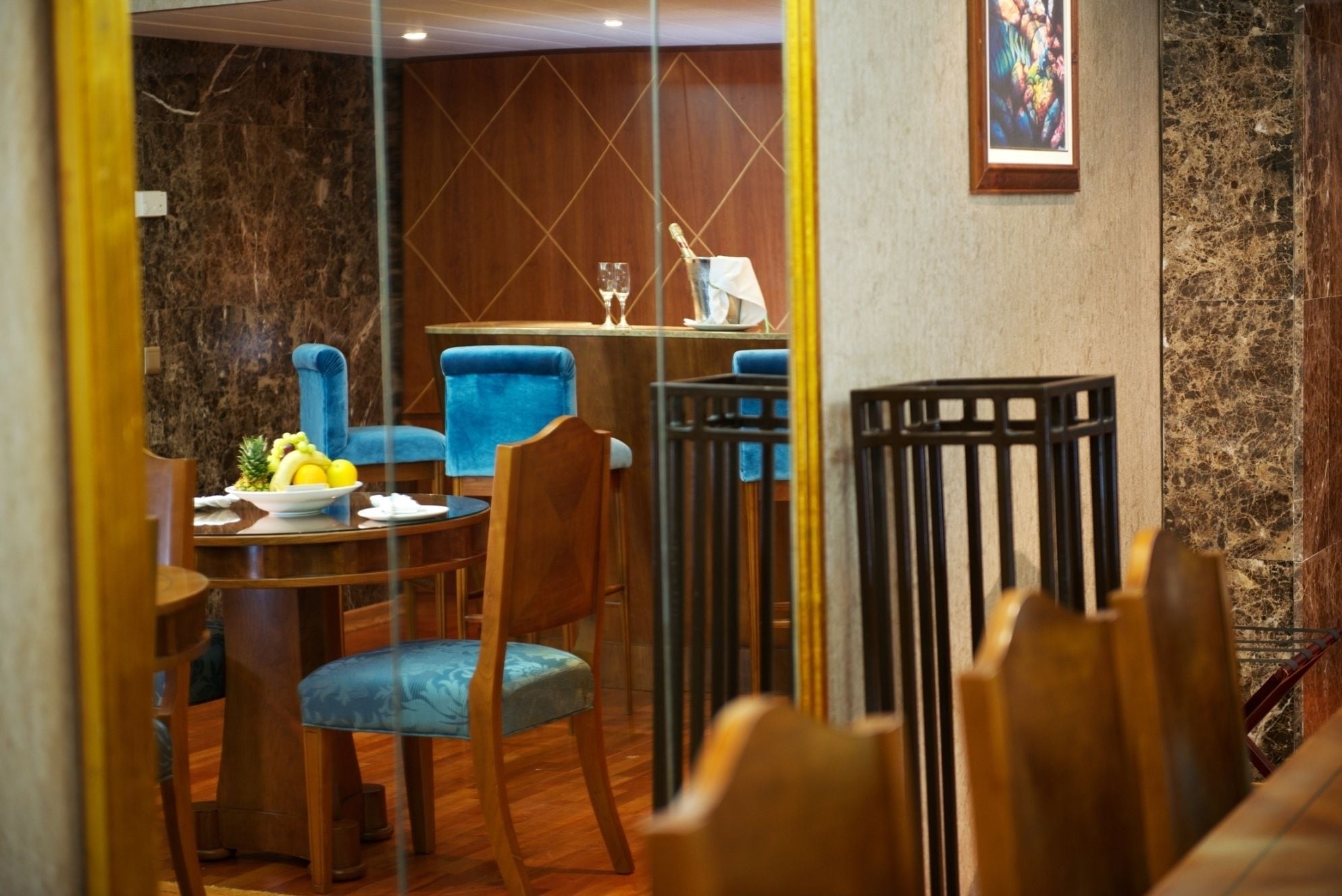 Restaurante com mesa de madeira, cadeiras azuis e divisória de vidro.