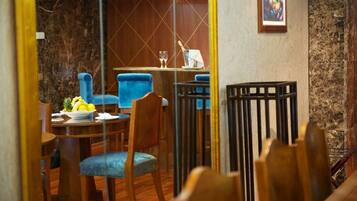 Restaurante com mesa de madeira, cadeiras azuis e divisória de vidro.