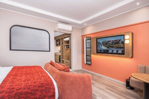 Quarto de hotel com cama, área de estar, guarda-roupa e televisão presa à parede.