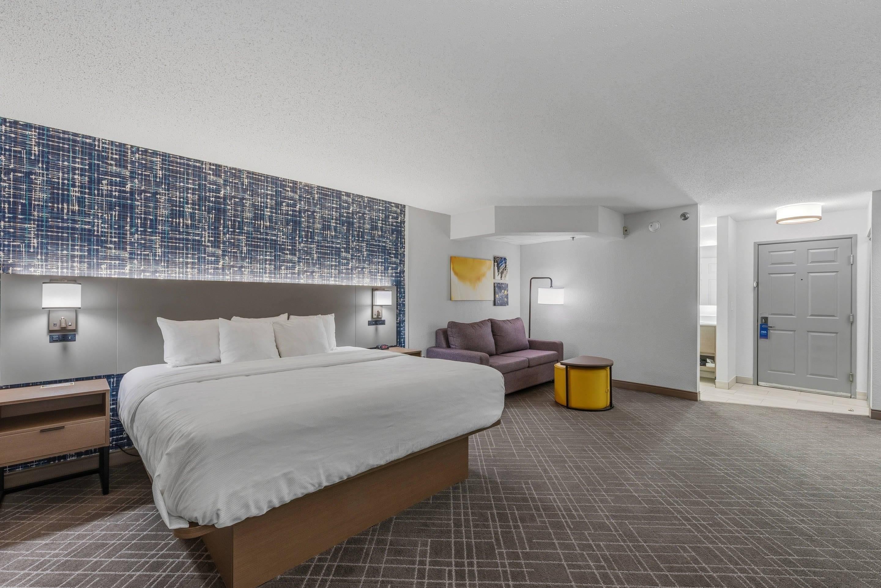 Quarto de hotel com uma cama grande, um sofá, uma mesinha e uma parede com design abstrato azul.