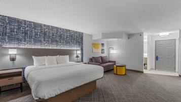 Quarto de hotel com uma cama grande, um sofá, uma mesinha e uma parede com design abstrato azul.