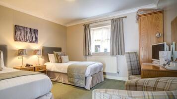 Quarto de hotel com duas camas, uma escrivaninha com computador, uma cadeira e uma janela com cortinas.