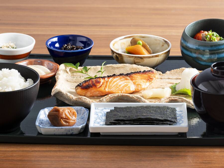 Uma bandeja com diversos pratos japoneses, incluindo salmão, arroz e alga.