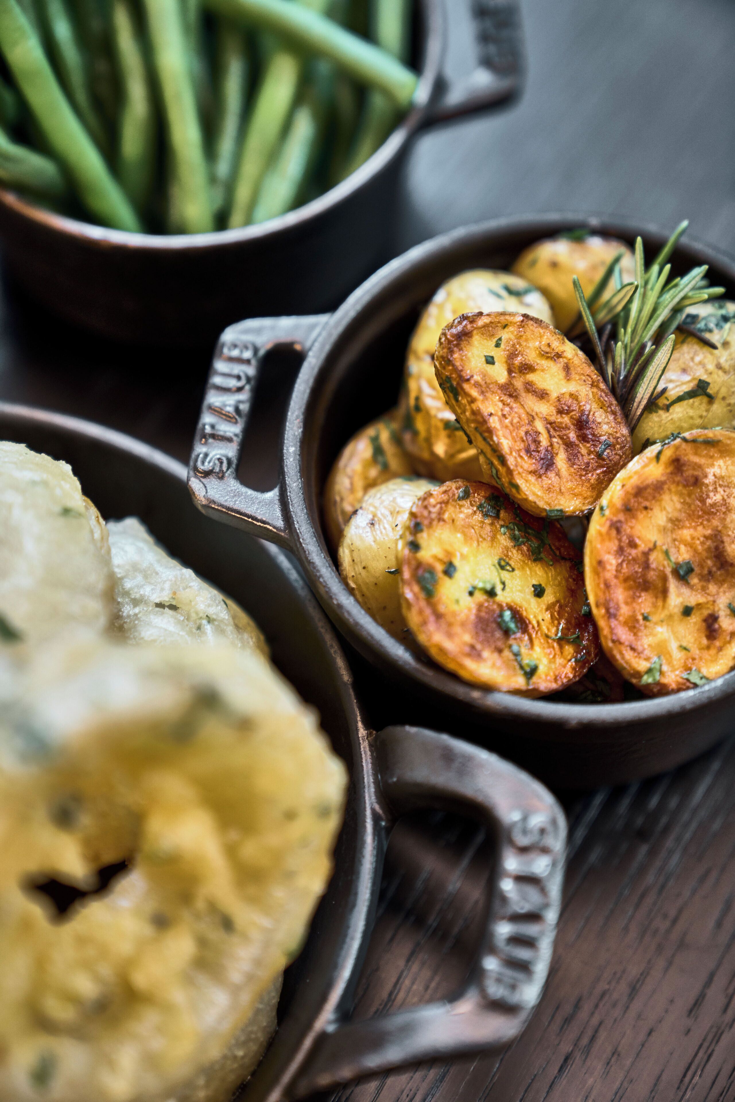 Close-up de uma frigideira de ferro fundido com batatas assadas e um acompanhamento de vagem.