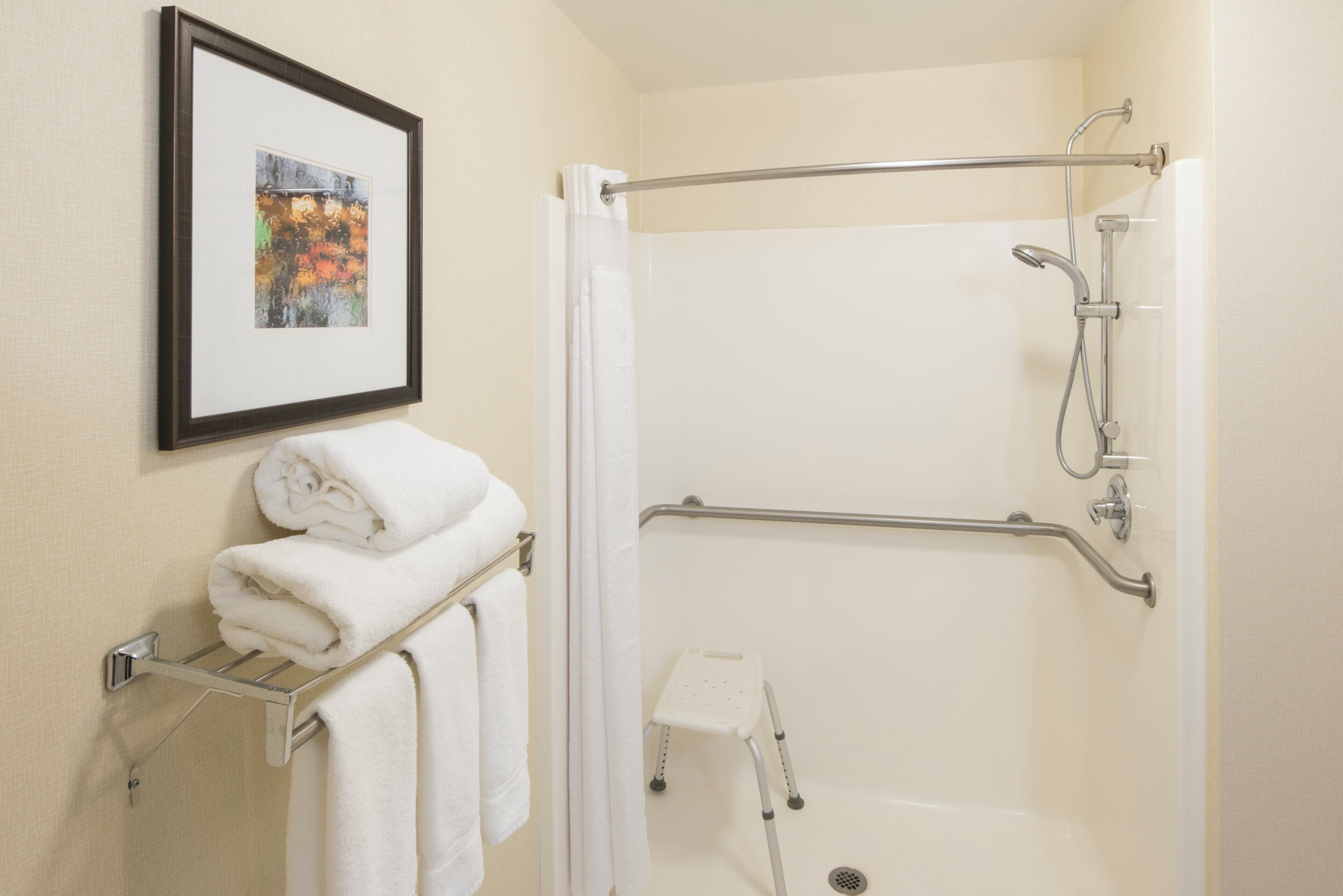 Casa de banho com chuveiro, porta-toalhas com toalhas dobradas e um quadro na parede.