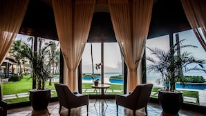 Quarto com duas cadeiras viradas para uma janela ampla com vista para uma piscina e um jardim.