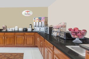 Uma cozinha com armários de madeira, bancada preta, cafeteira, torradeira e uma tigela de maçãs.
