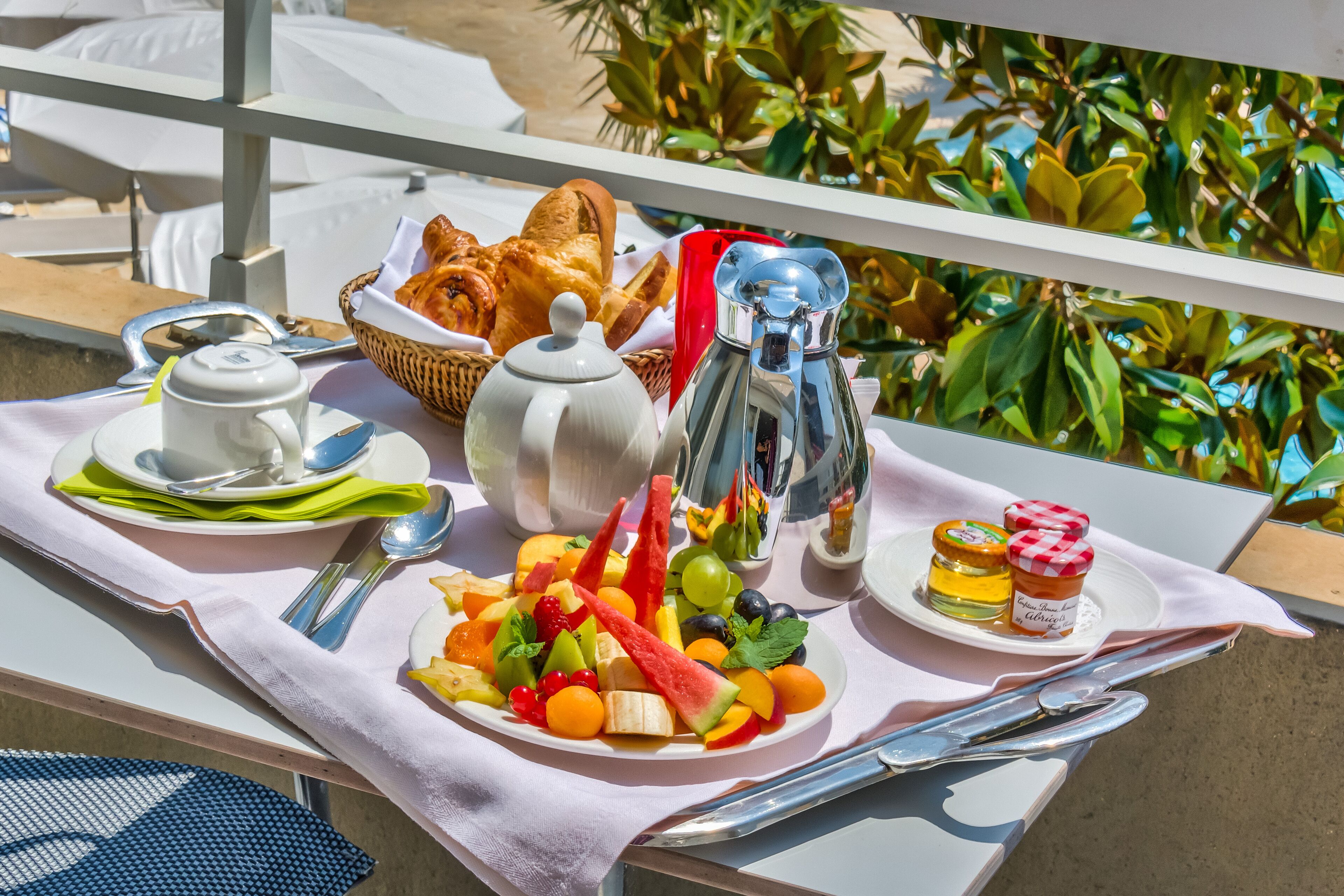 Mesa posta com itens de café da manhã, incluindo pão, frutas, um bule e acompanhamentos.