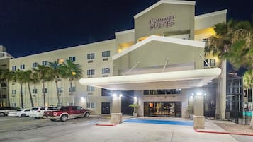 Entrada de hotel com placa indicando "Comfort Suites", área de estacionamento coberta e um edifício com várias janelas.