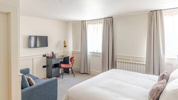 Quarto de hotel com cama, escrivaninha, cadeira, televisão e janela com cortinas.