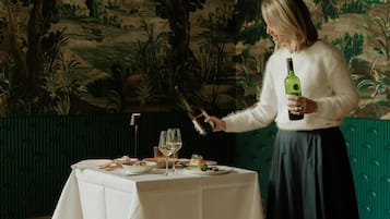 Uma mesa de jantar com toalha branca, uma garrafa de vinho e um copo.