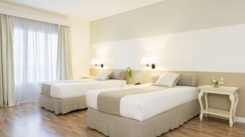 Quarto de hotel com duas camas, uma mesa pequena e uma mesinha de cabeceira com abajures.