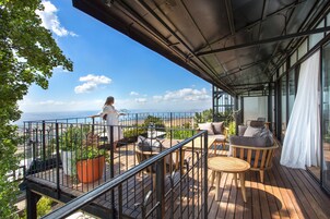 Varanda com vista para o mar, mobiliada com cadeiras e uma mesa, e um corrimão.
