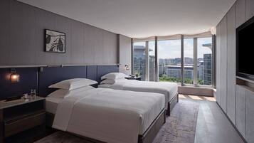 Quarto moderno com duas camas, uma janela grande com vista para a cidade e uma televisão montada.