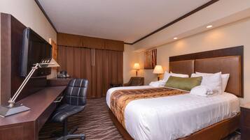 Quarto de hotel com uma cama grande, uma escrivaninha com cadeira, uma TV de tela plana e um abajur.