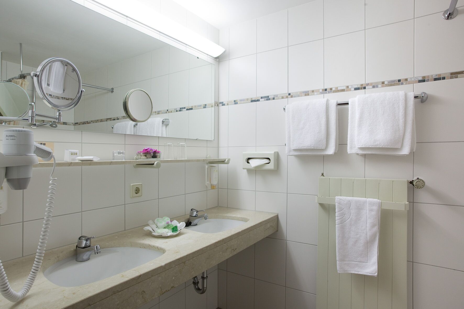 Casa de banho com duas pias, um espelho, um secador de cabelo e um porta-toalhas.