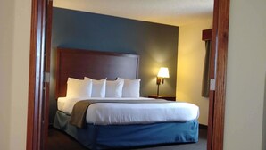 Quarto de hotel com uma cama, uma mesa de cabeceira e uma luminária, e uma moldura de madeira na porta.