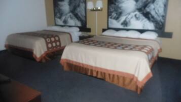 Quarto de hotel com duas camas, uma mesinha de cabeceira e uma luminária.