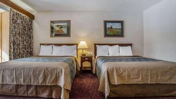 Quarto de hotel com duas camas, uma mesa de cabeceira com abajur e duas imagens emolduradas na parede.