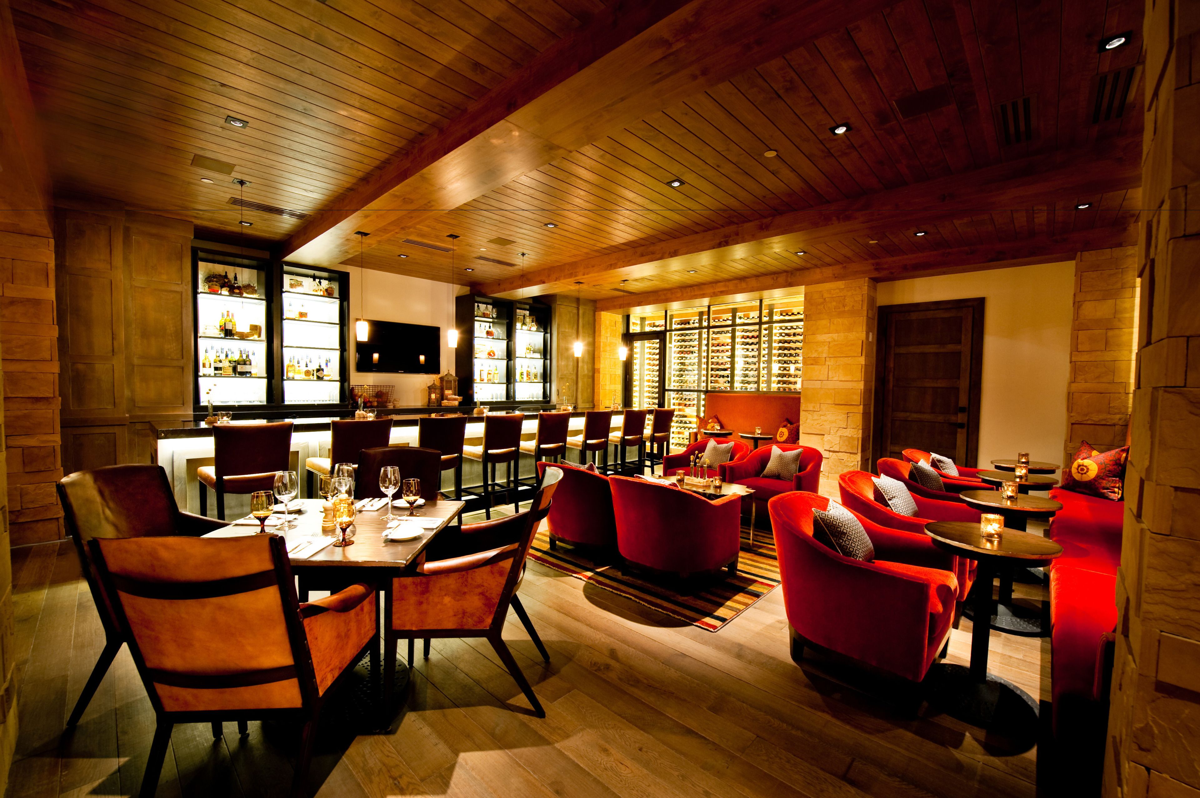 Restaurante com teto de madeira, assentos vermelhos e área de bar com prateleiras de garrafas.