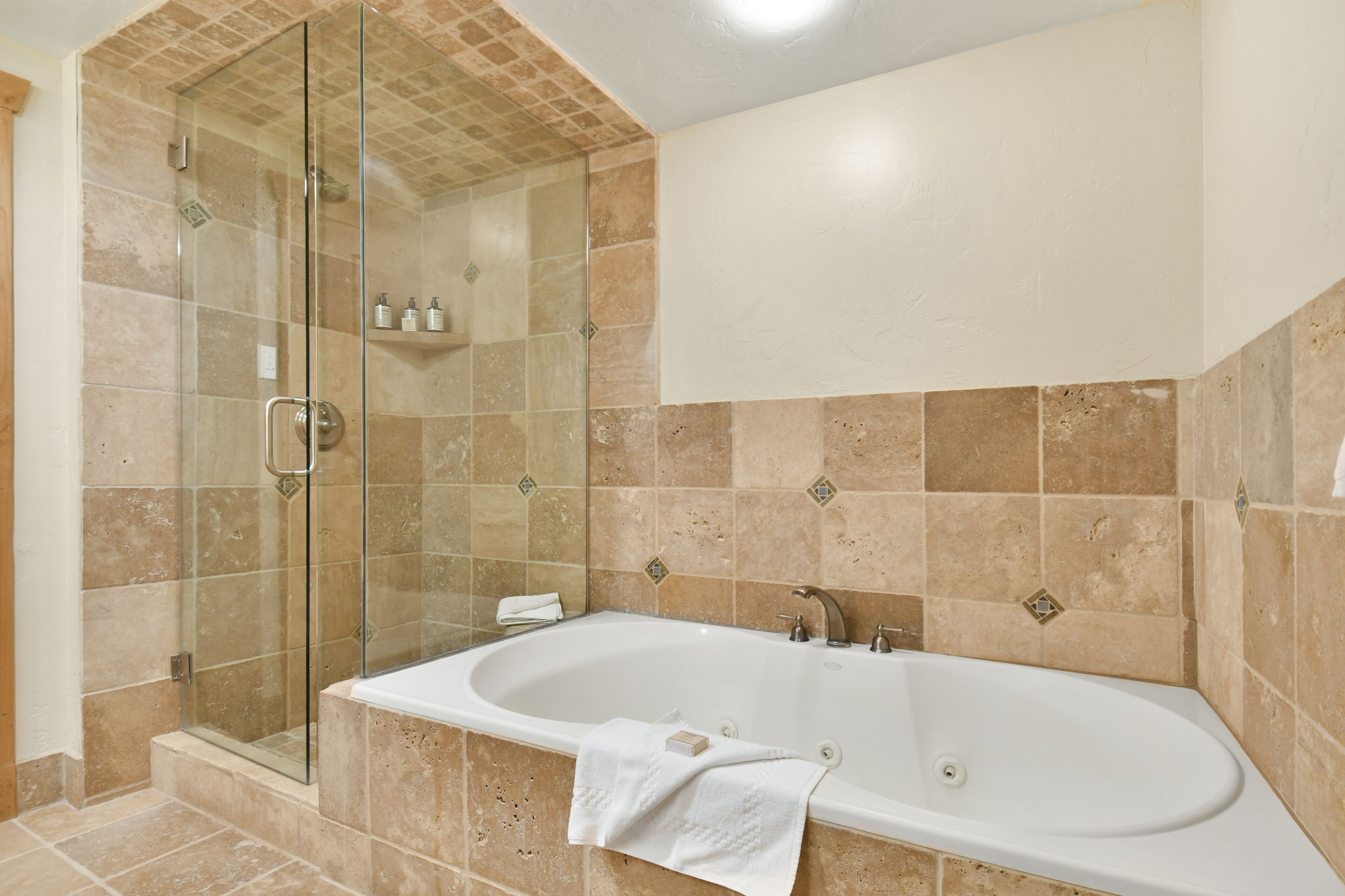 Um banheiro moderno com chuveiro em box de vidro, banheira de pedestal e paredes revestidas com azulejos bege.