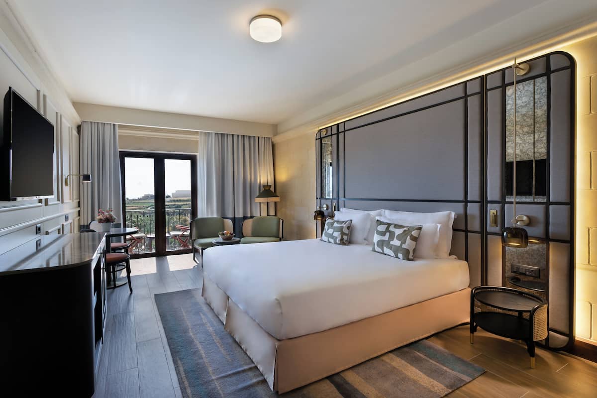 Quarto de hotel com cama grande, escrivaninha, cadeira, televisão e varanda com vista.